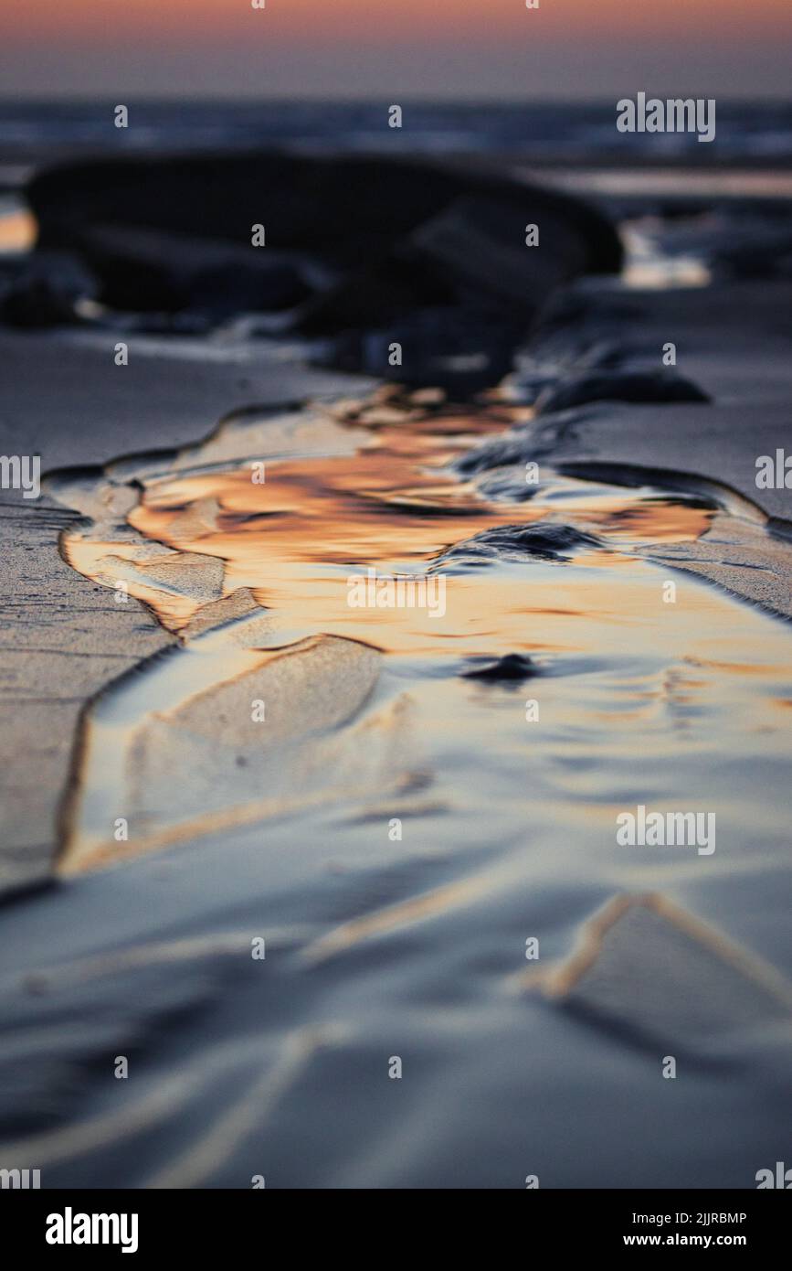 A vertical shot of cracks on the sand filled with water on the shore of ...