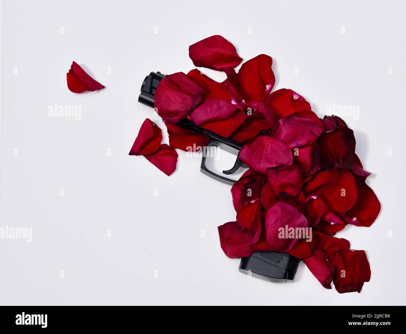 A top view of a gun covered in red rose petals on a white background ...
