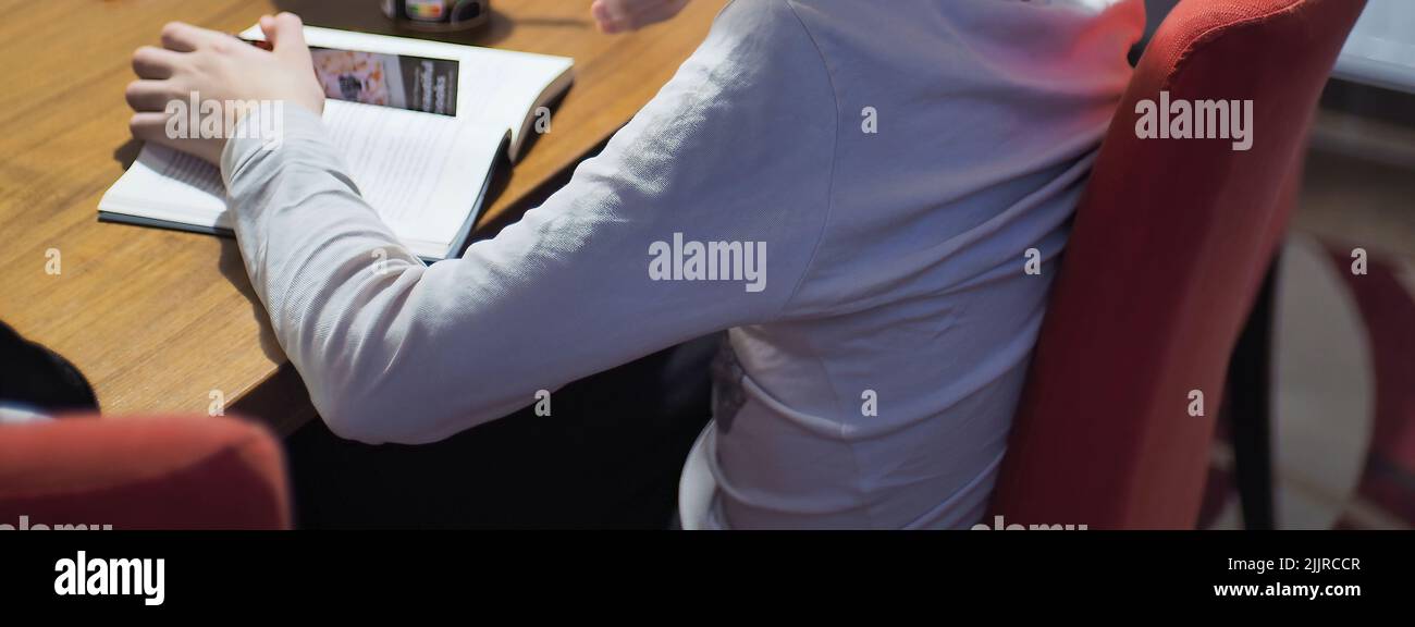 A closeup of faceless man with open book on red chair in book group ...