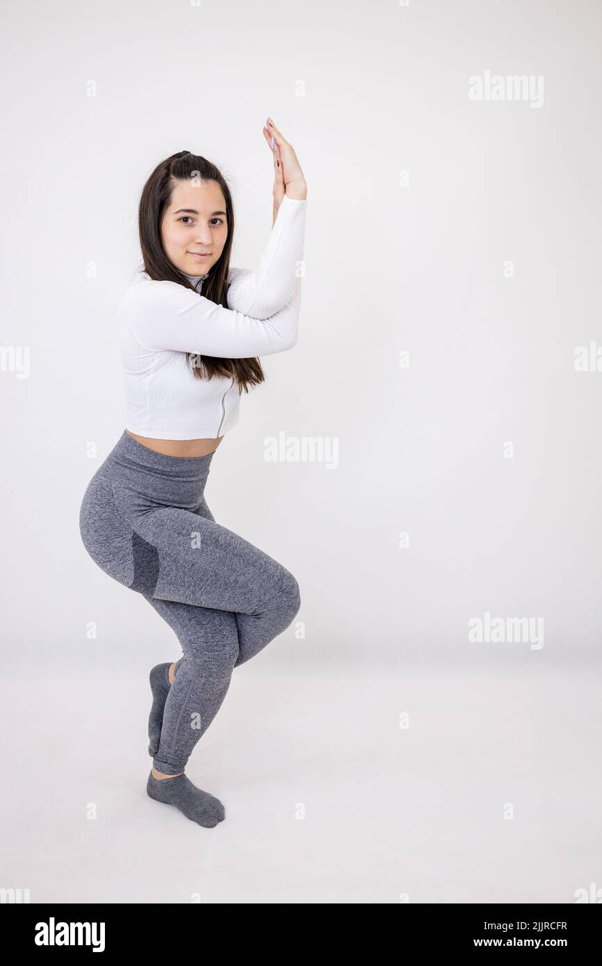 A vertical shot of a young woman posing for yoga exercises on a light ...