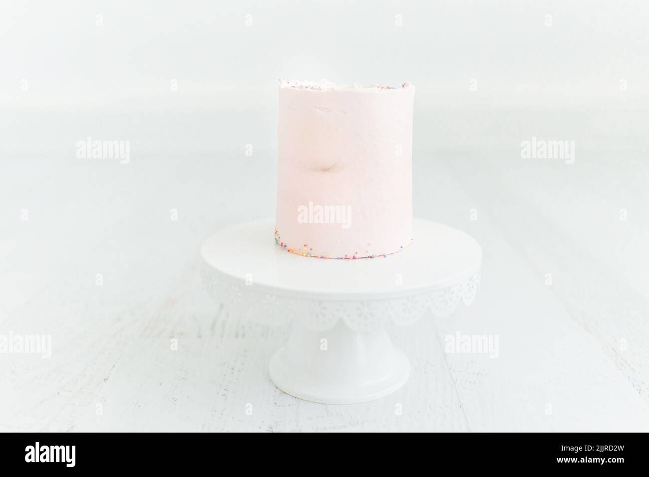 A side view of a light pink cake on a stand on white background Stock ...