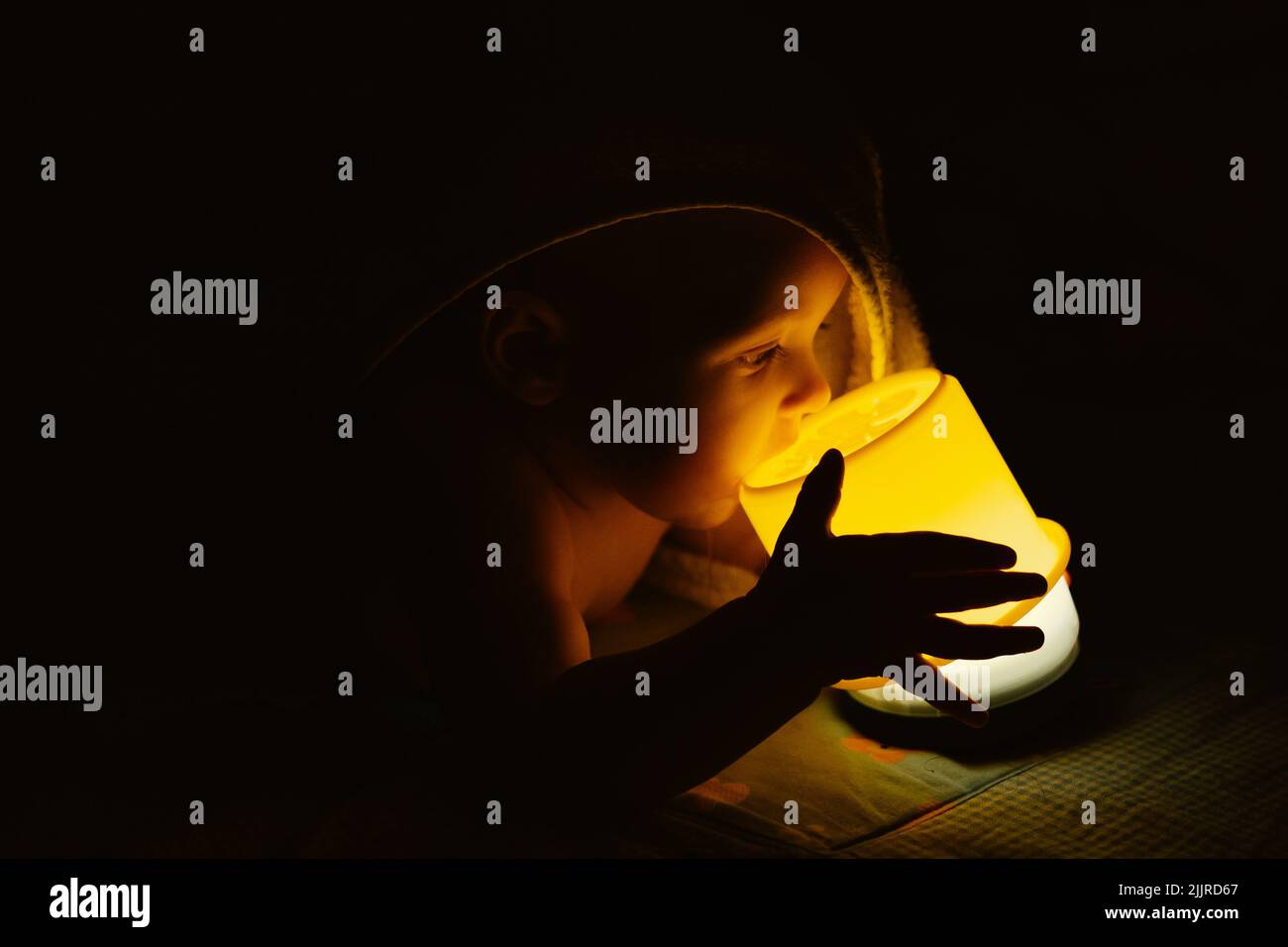 A close-up shot of a baby holding a yellow lightbox in the dark Stock ...