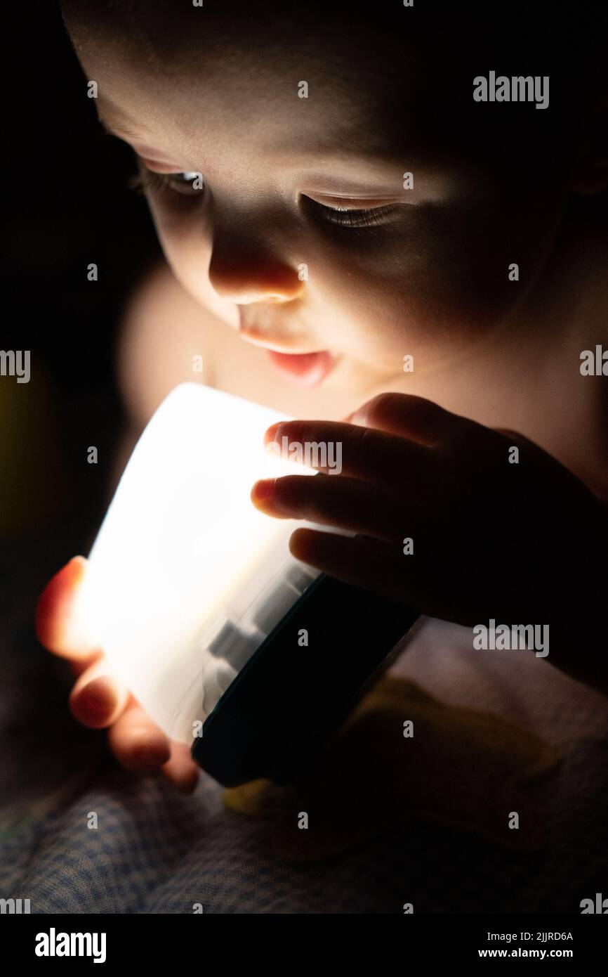 A vertical closeup of a baby girl holding a light in a dark room Stock ...
