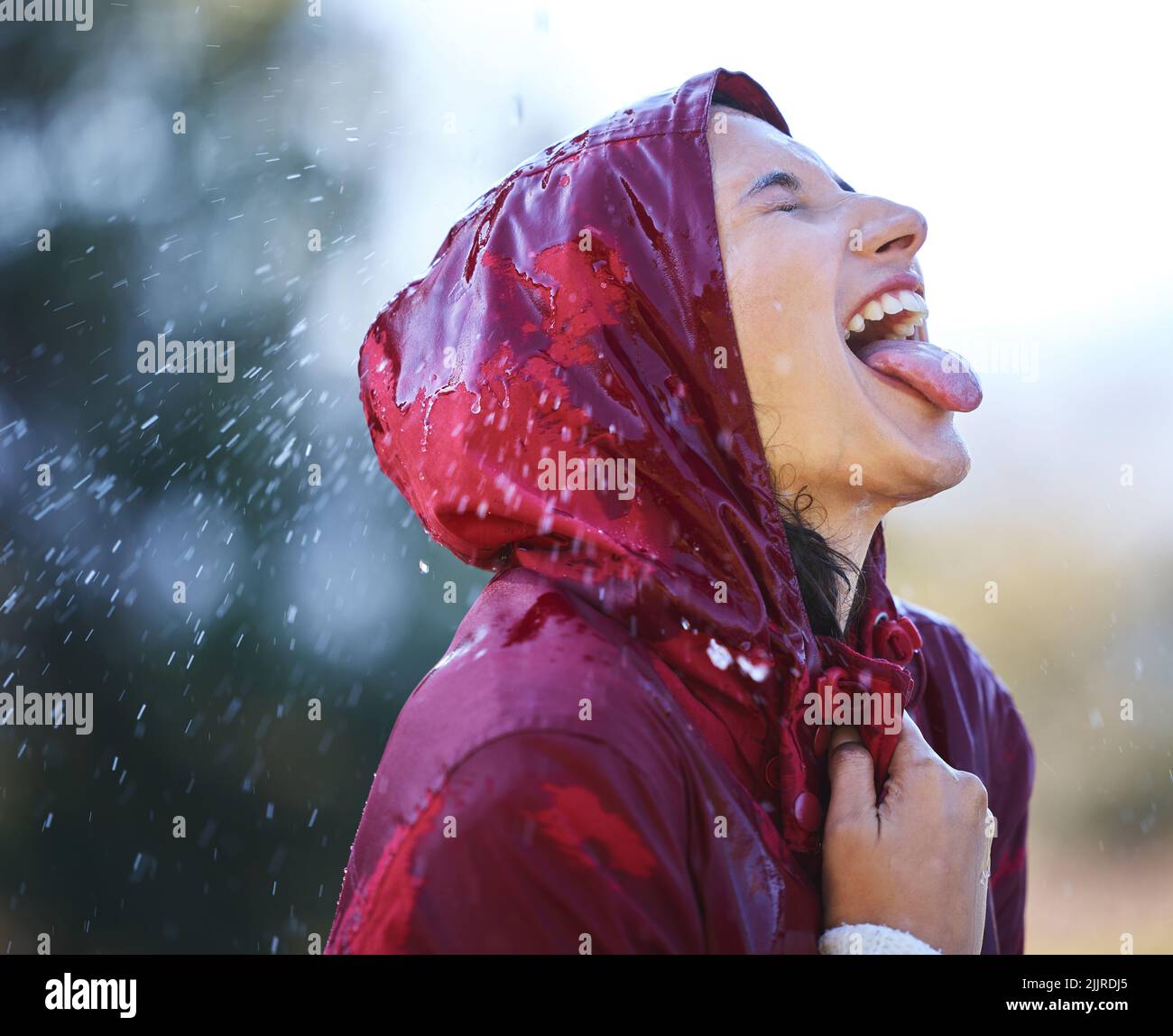 Carefree in the rain. a young woman sticking out her tongue to feel the ...