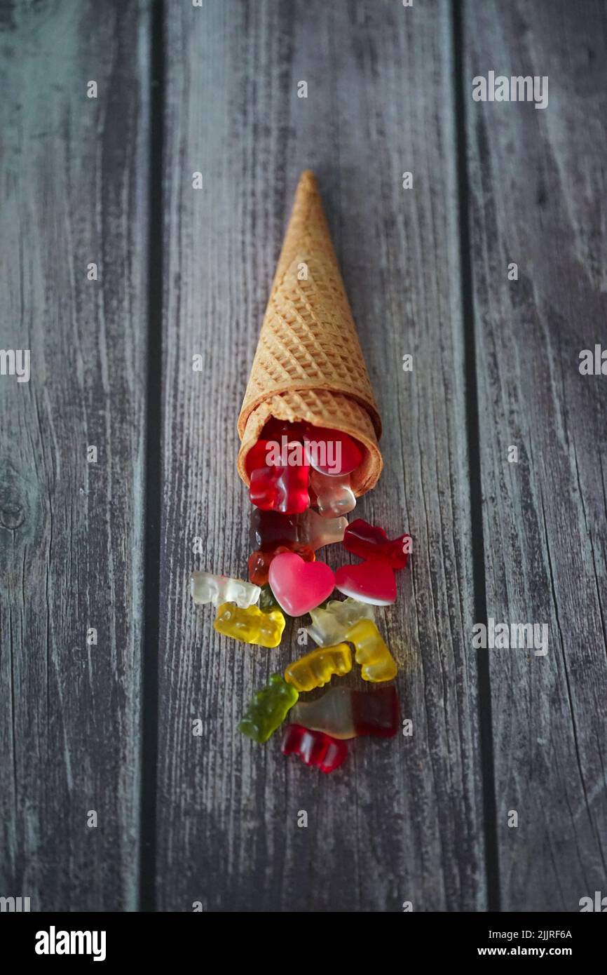 The colorful gummy bears and the hearts by the waffle cone on a wooden ...