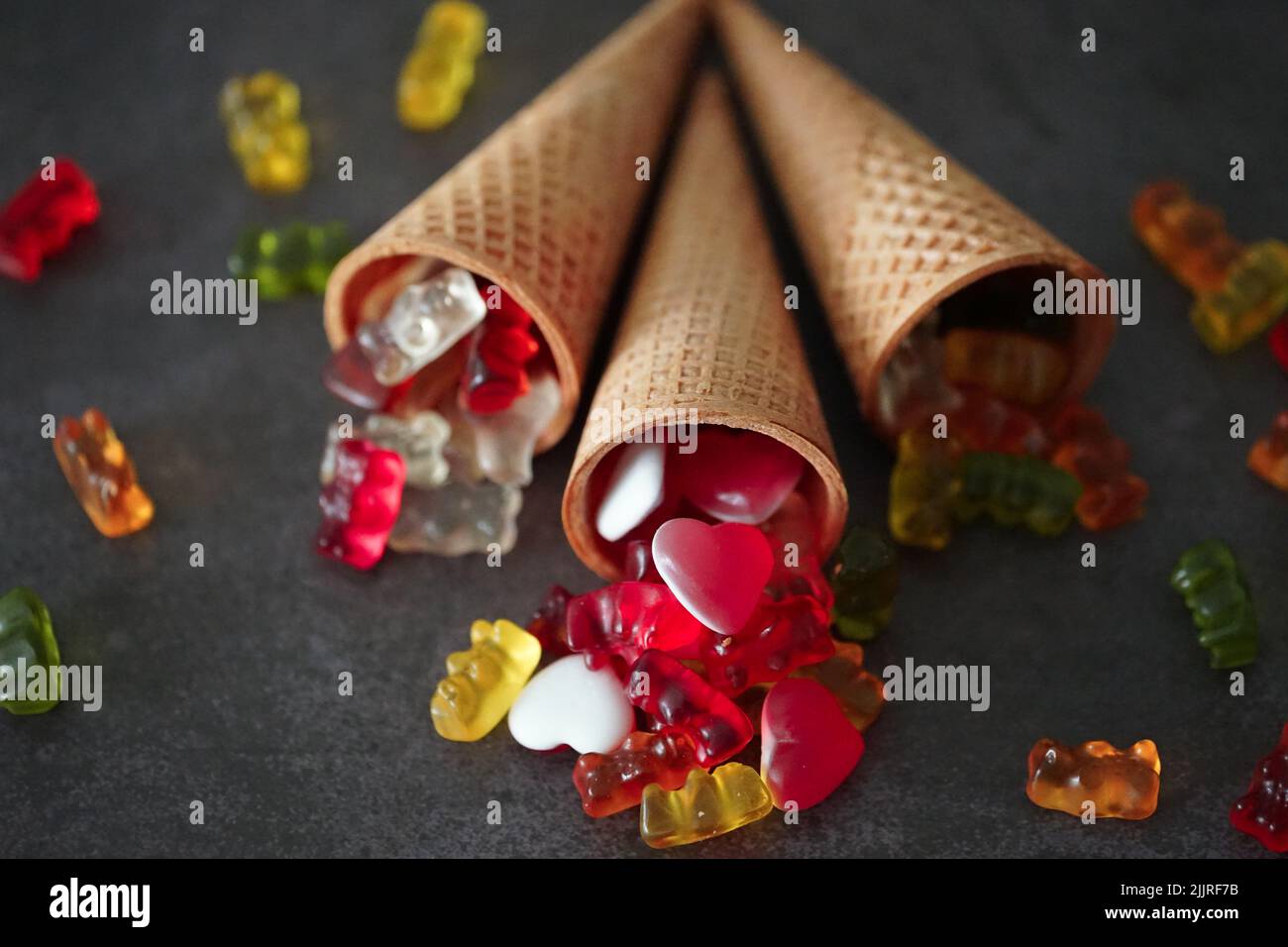 The colorful gummy bears and the hearts by the waffle cones on a black ...