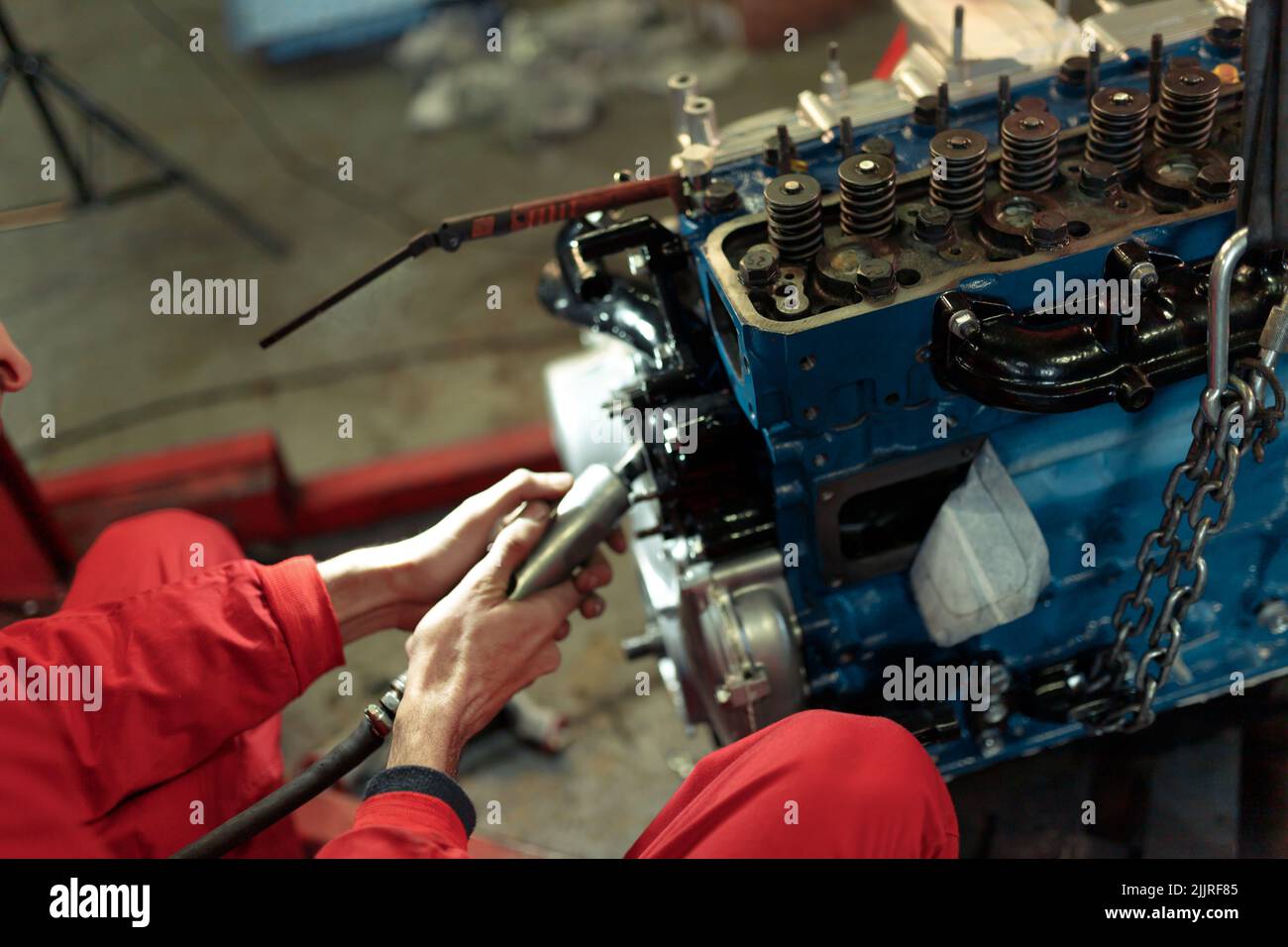 A closeup shot of a mechanic in a red uniform mounting the car engine ...