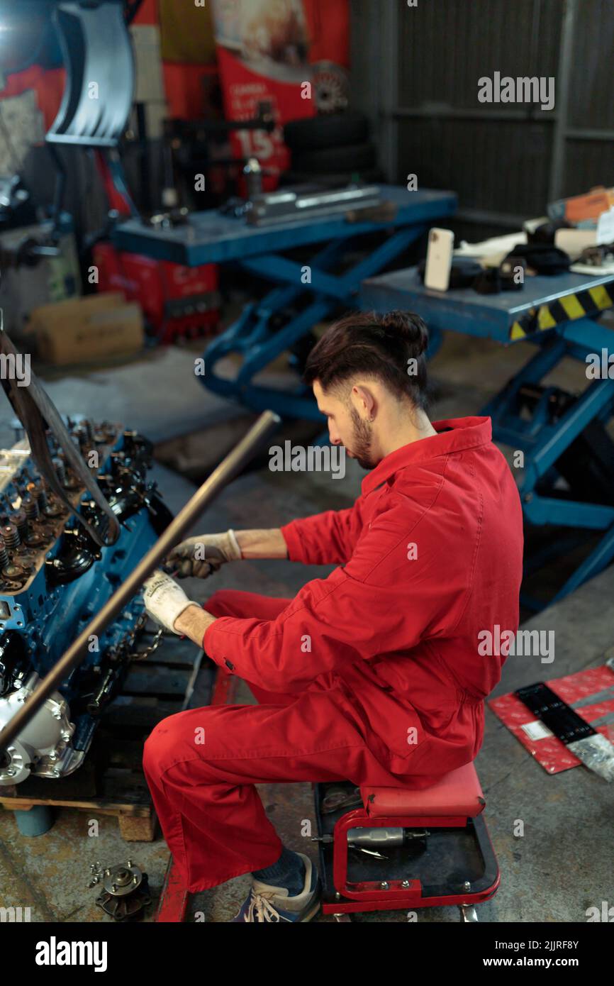A vertical shot of a young Caucasian mechanic in a red uniform mounting ...