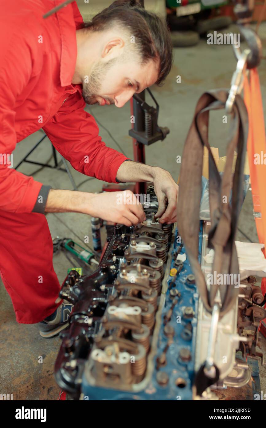 A vertical shot of a young Caucasian mechanic in a red uniform mounting ...