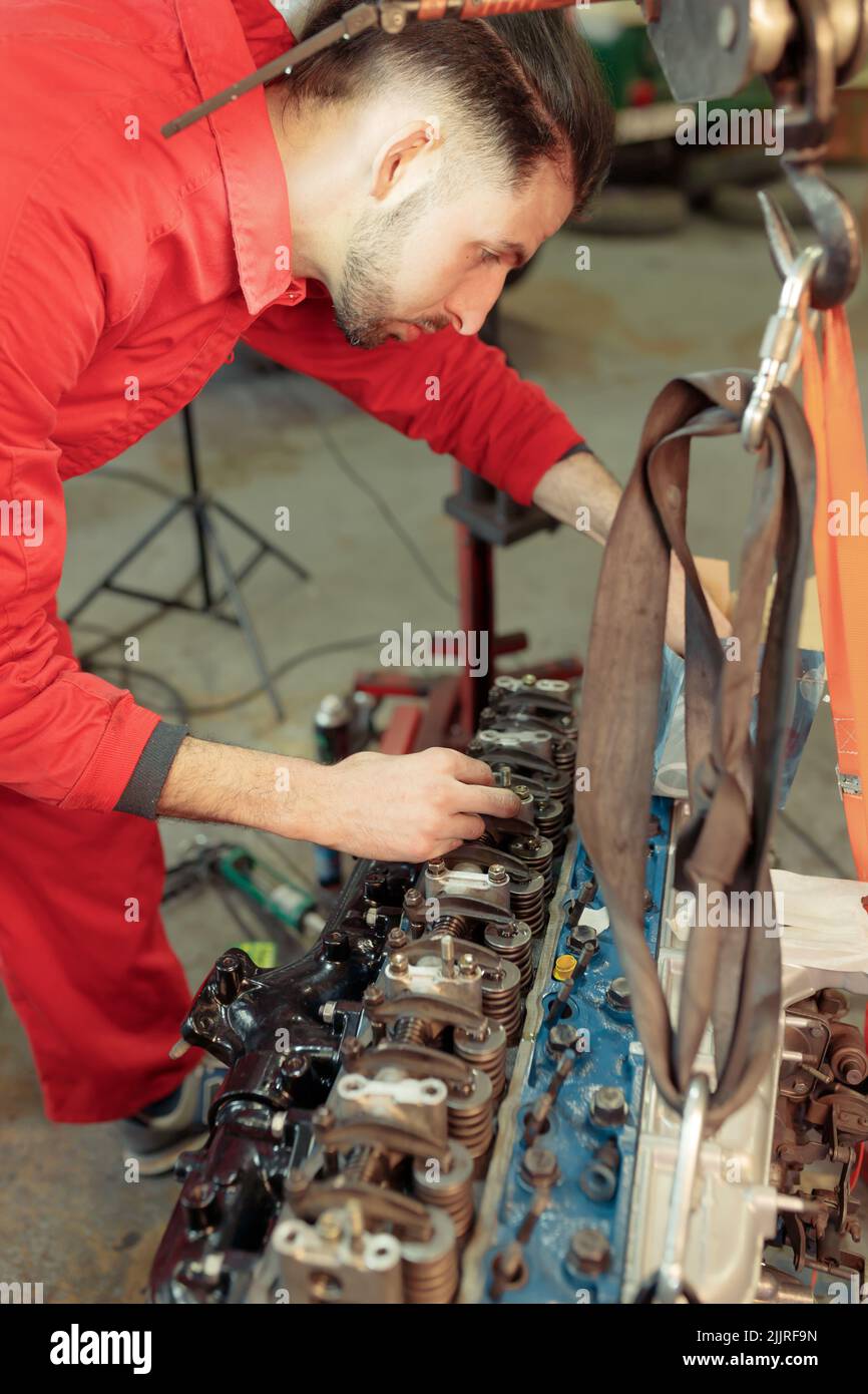 A vertical shot of a young Caucasian mechanic in a red uniform mounting ...