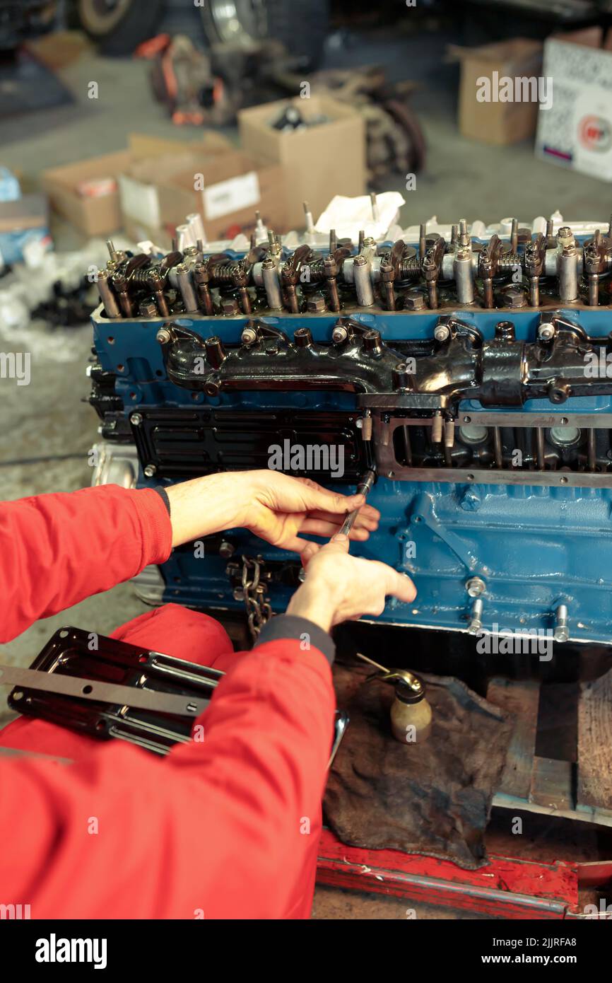 A vertical closeup shot of a young mechanic in a red uniform mounting ...