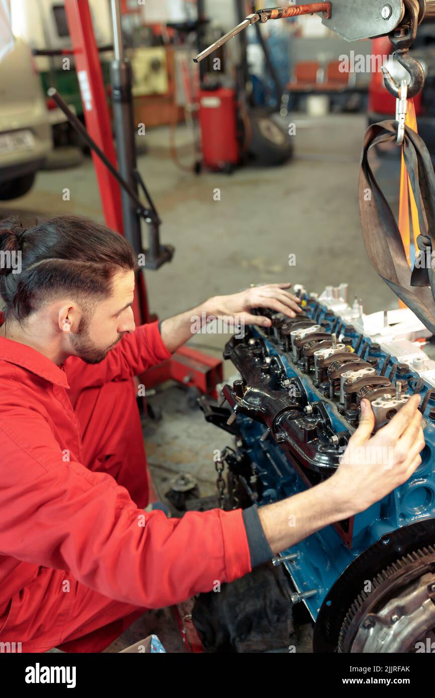 A vertical closeup shot of a young Caucasian car mechanic in a red ...