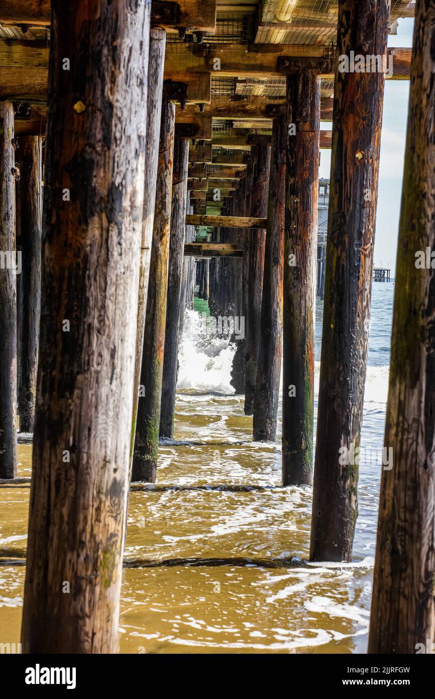 A vertical shot of wooden pillars of a deck with waves washing the ...