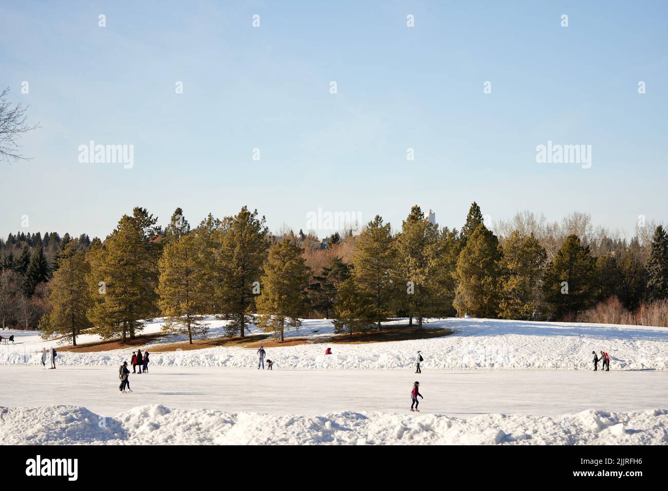 A winter landscape with people ice skating on a rink surrounded by a ...