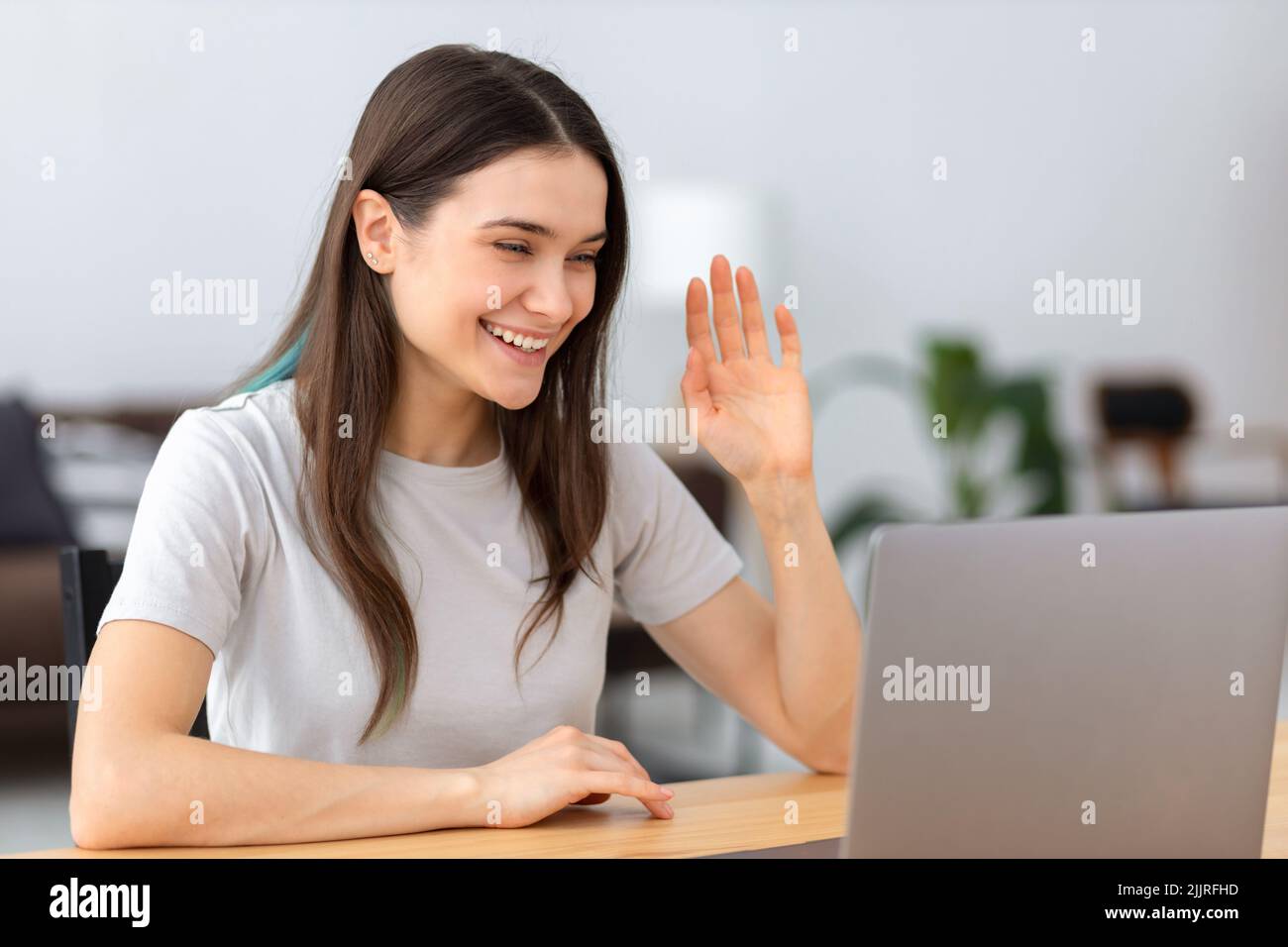 Smiling woman waving hand showing greeting gesture, looking at laptop ...