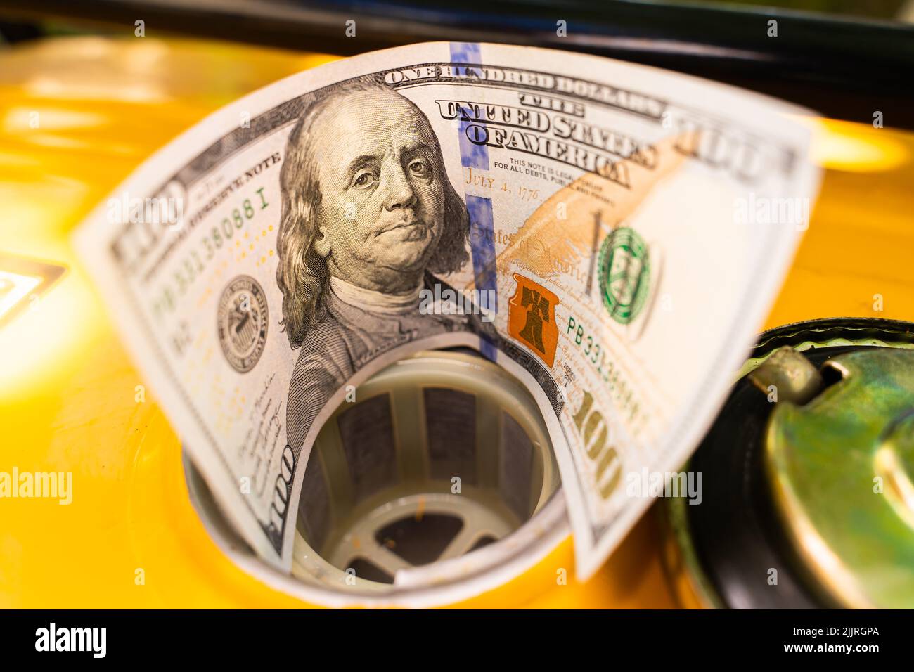 A close-up of a one hundred dollar bill in a fuel filler neck in a ...