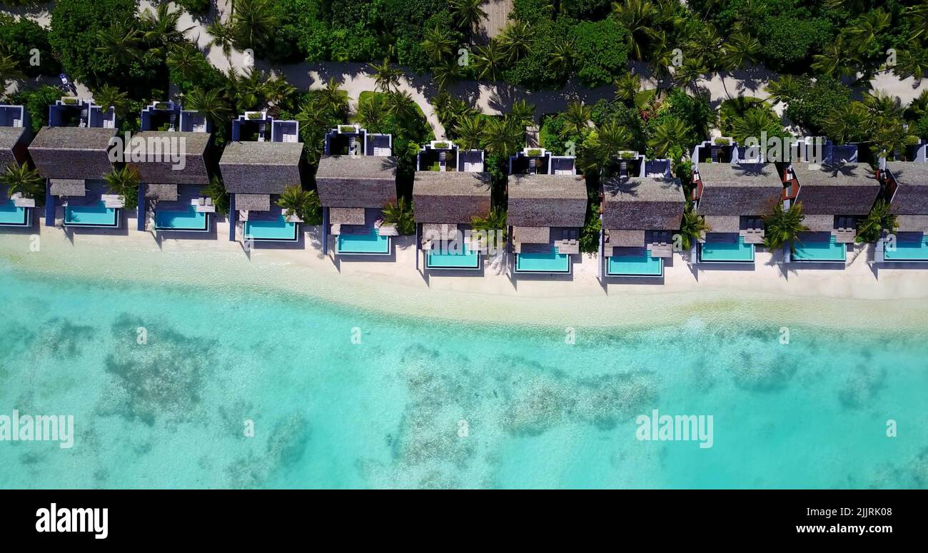 An aerial view of bungalows with swimming pools on sandy beach in ...