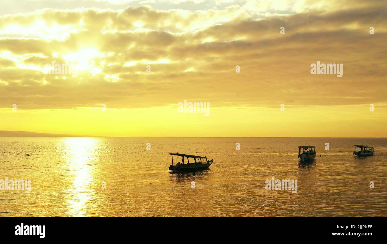 A scenic view of boats sailing in a sea reflecting the golden sunset ...