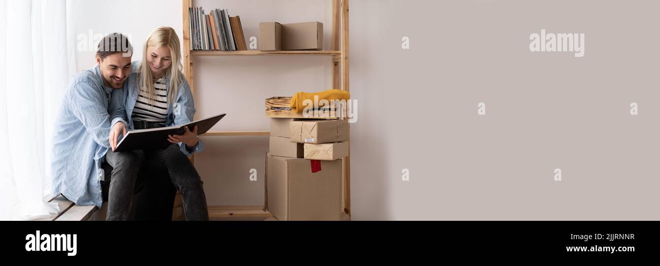 Happy couple looking at photo album while unpacking stuff after ...