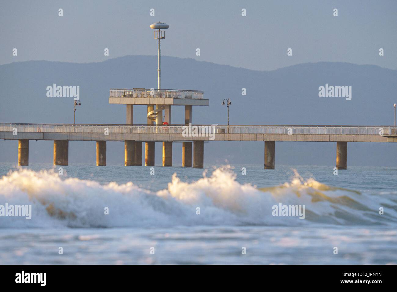 A beautiful shot of a bridge in the background of the sea waves and a ...