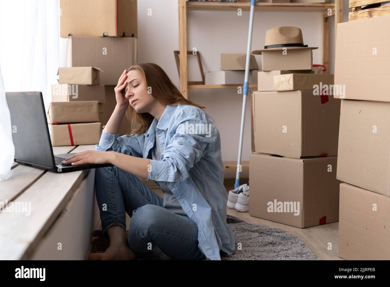 Young worried unhappy woman sitting on the floor near moving boxes ...