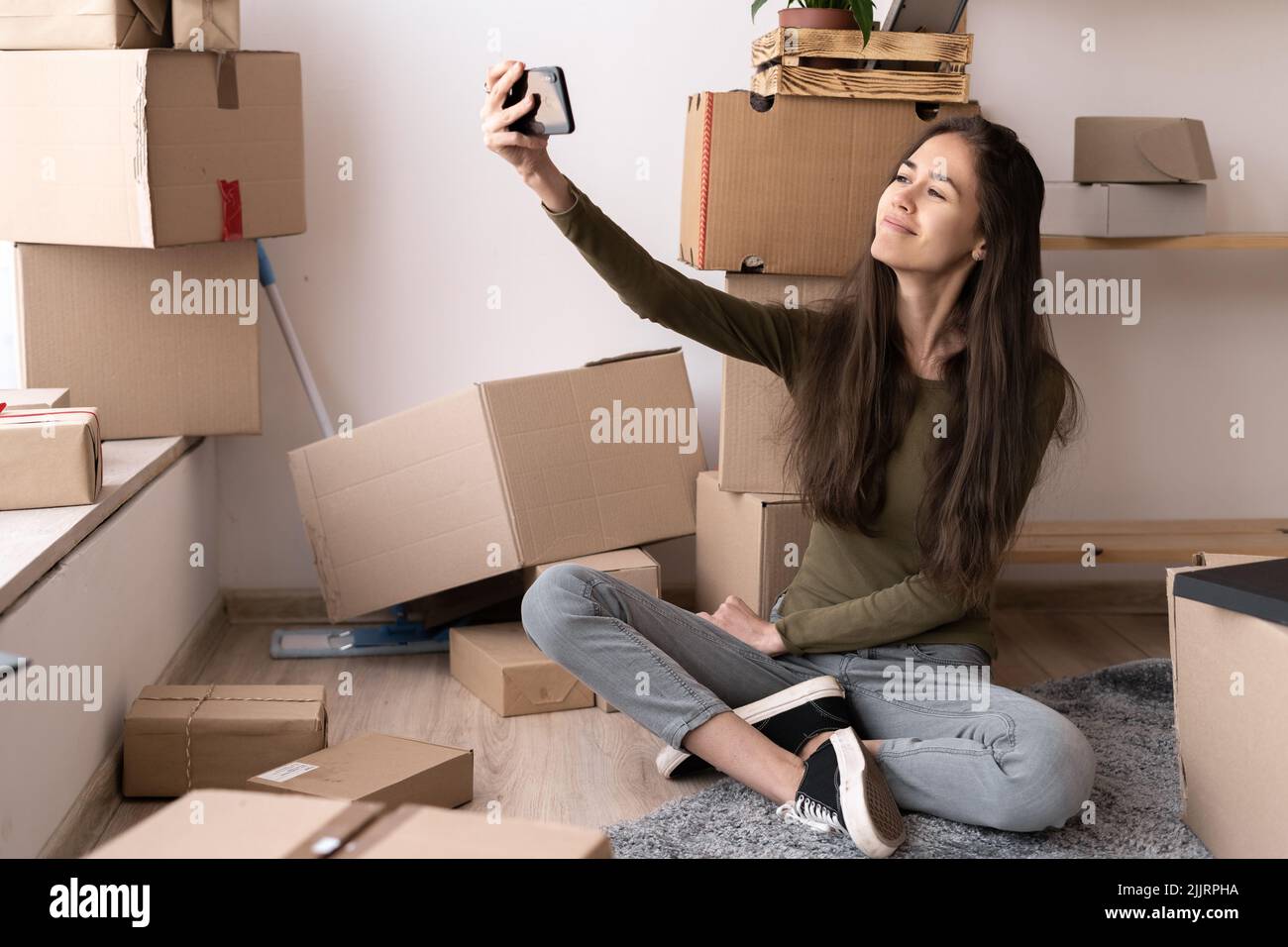 happy brunette girl taking selfie with smartphone and sitting on floor ...