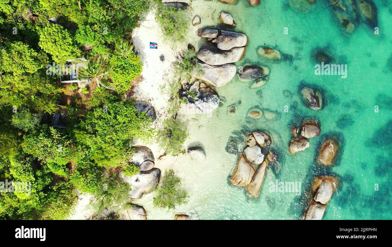 An aerial view of a beach with trees, big rocks and turquoise water in ...