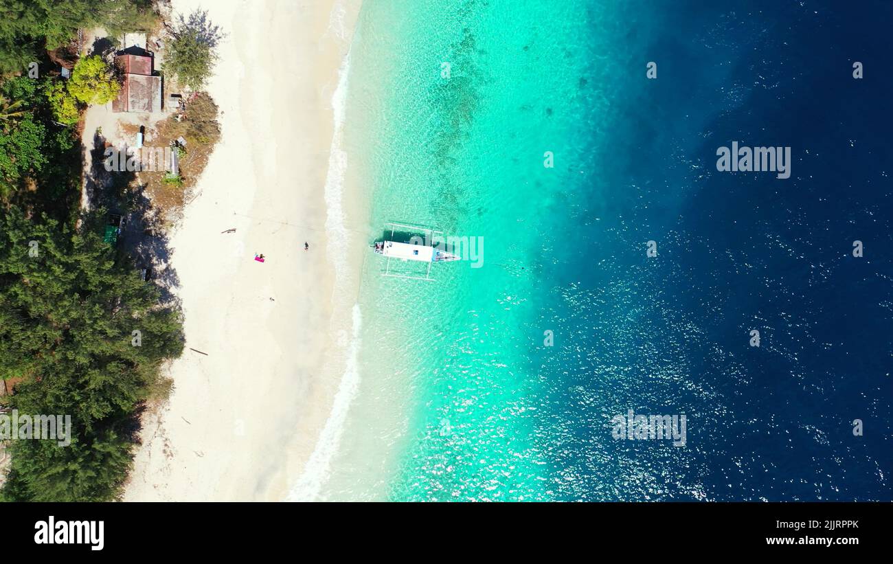 An aerial top view of a yacht floating in turquoise water by a beach in ...