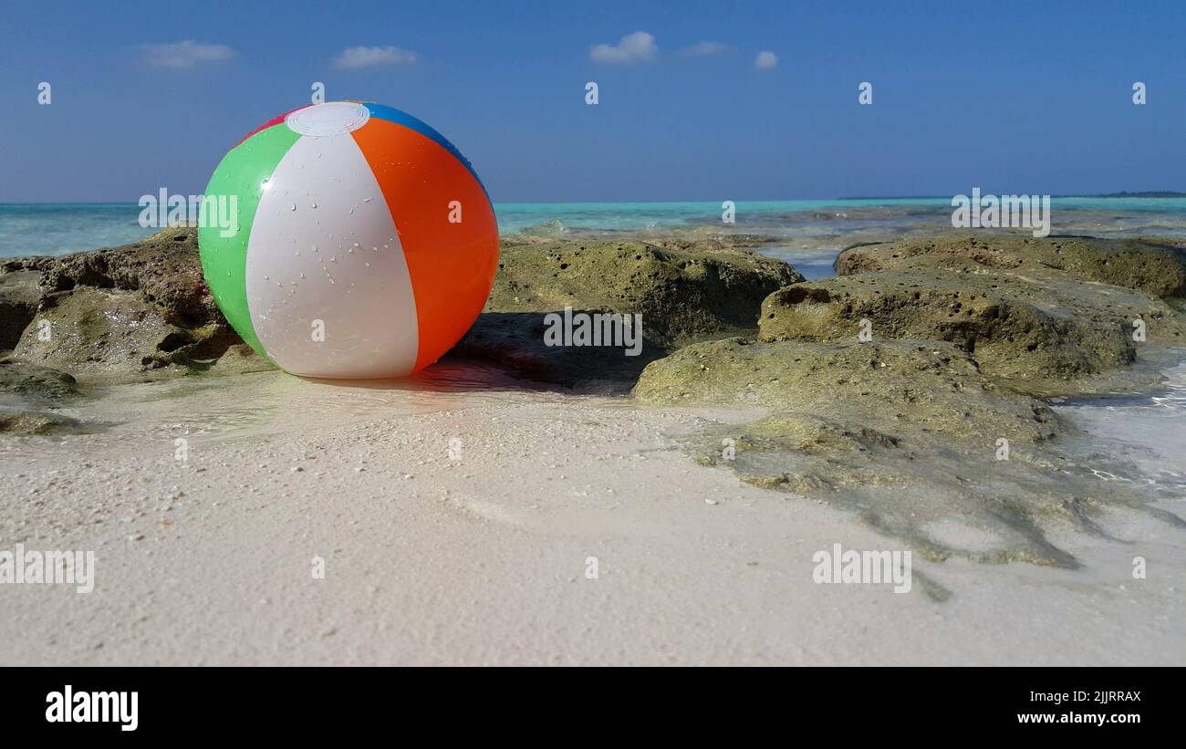 A closeup shot of a beach ball on the rocky coastline with the clear ...