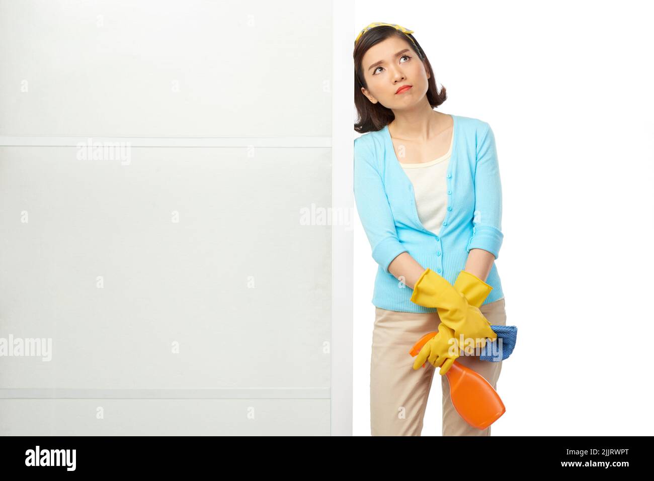 Pretty Asian housewife with detergent and rag in hands looking away ...
