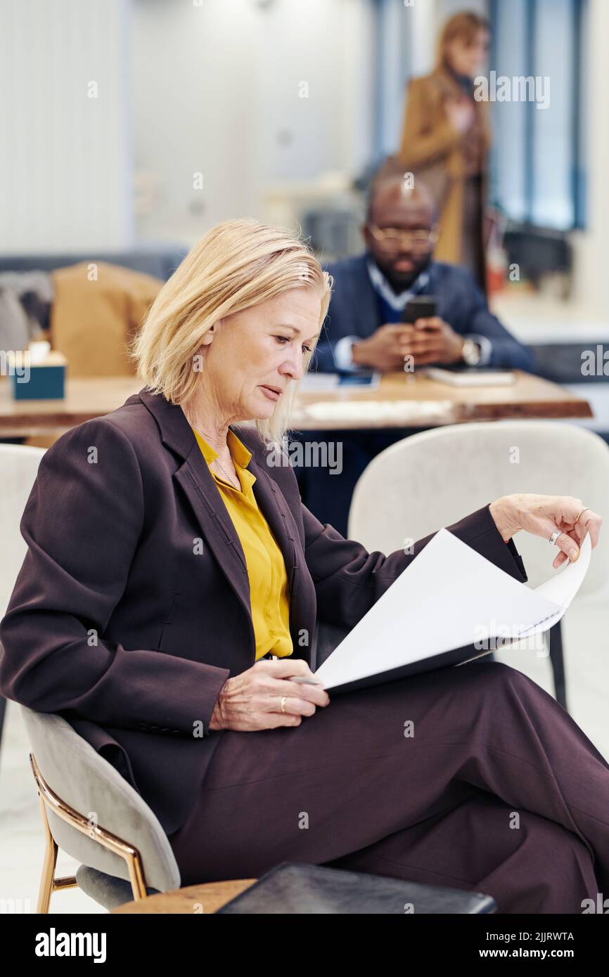 Mature female lawyer in suit sitting on chair and examining the ...