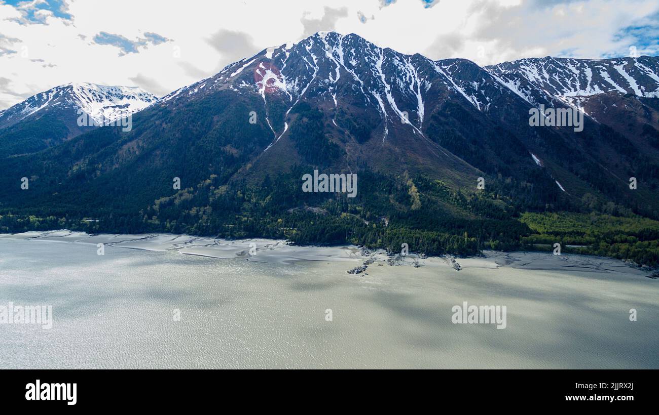 An aerial view of a snowy mountain range covered with clouds against a ...