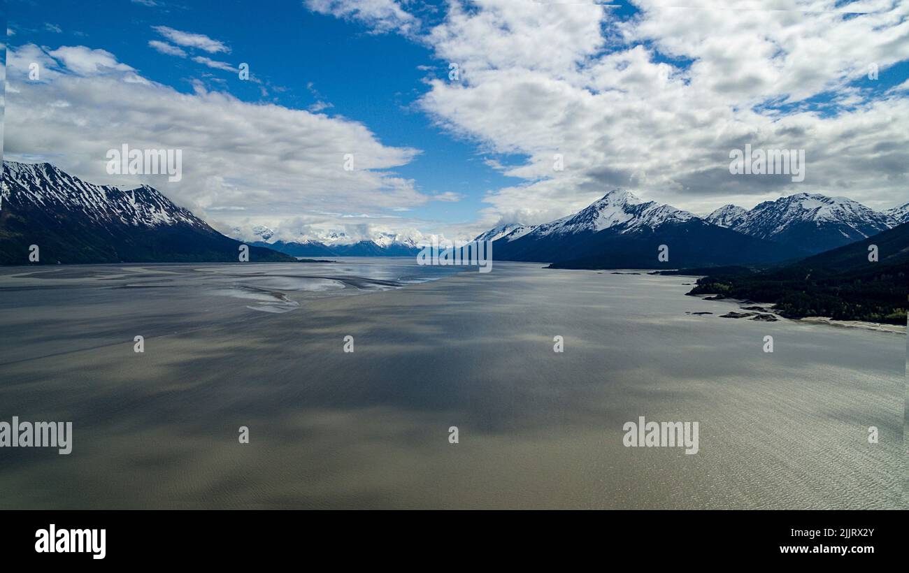 An aerial view of a snowy mountain range covered with clouds against a ...