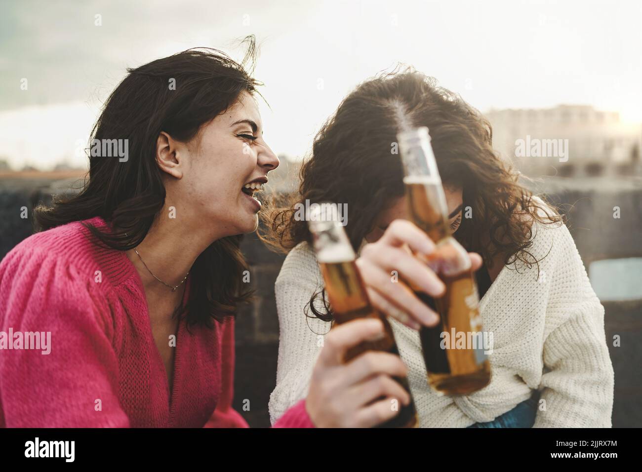 Two women having fun drinking beers outdoors laughing together - young ...