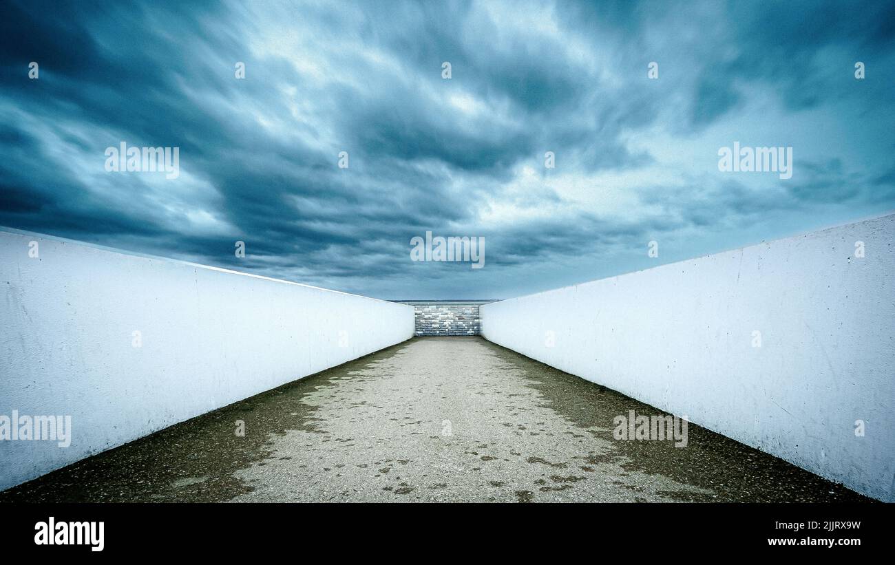A walking path in the middle of two white walls under a dramatic cloudy ...