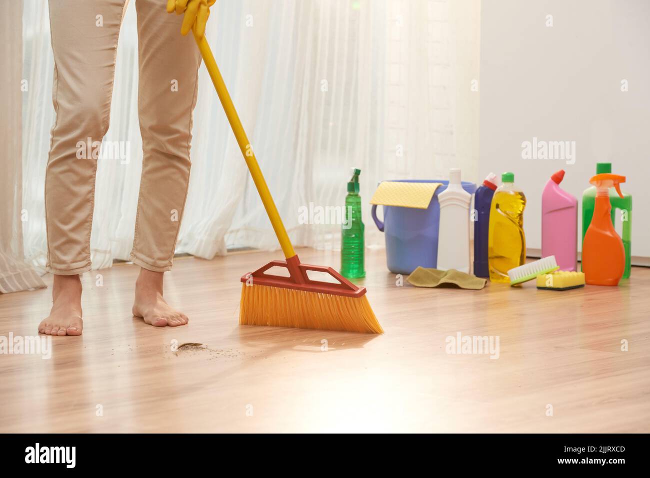 Unrecognizable barefoot woman sweeping floor with broom while wrapped ...