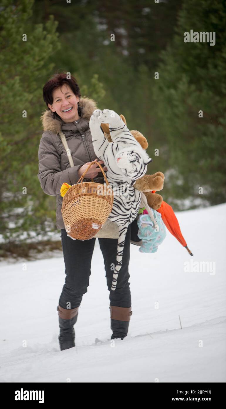 A Caucasian woman in winter outfit holding toys and basket in a snowy ...
