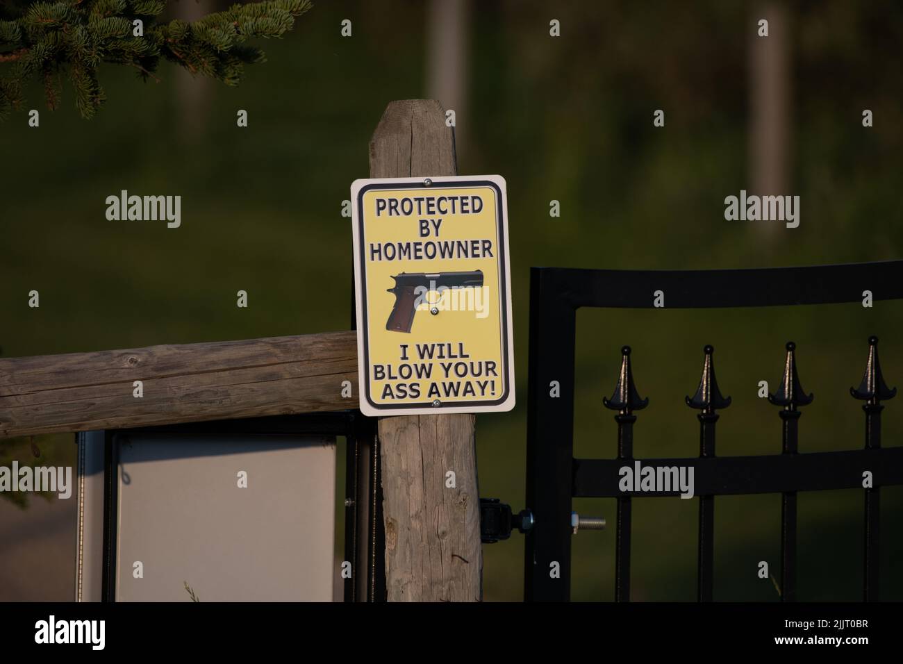 A close-up shot of a fence with a warning sign with a gun in the blurry ...