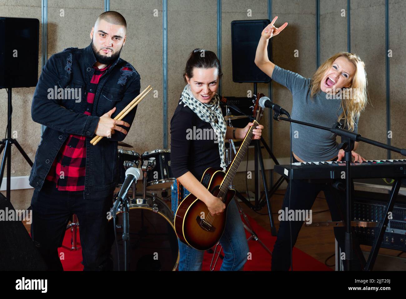 Three bandmates posing together with musical instruments in rehearsal ...