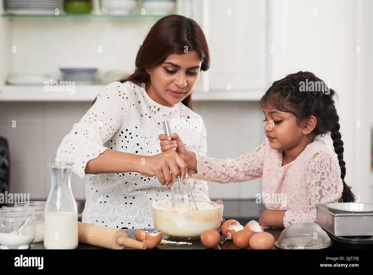 Cute Indian girl helping her beautiful middle-aged mother to beat eggs ...