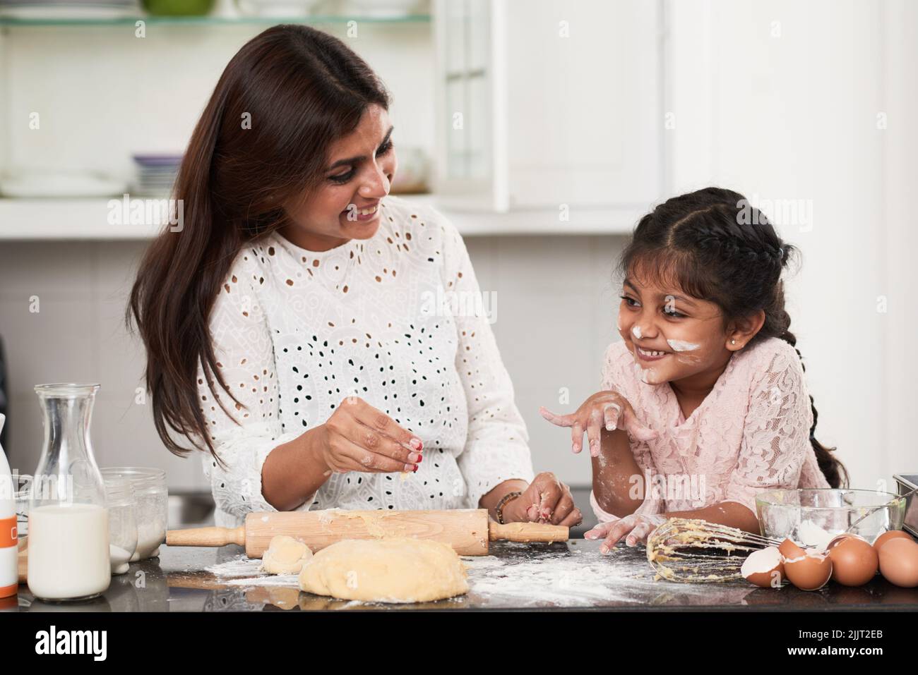 Smiling little girl with face smeared with flour looking away while ...