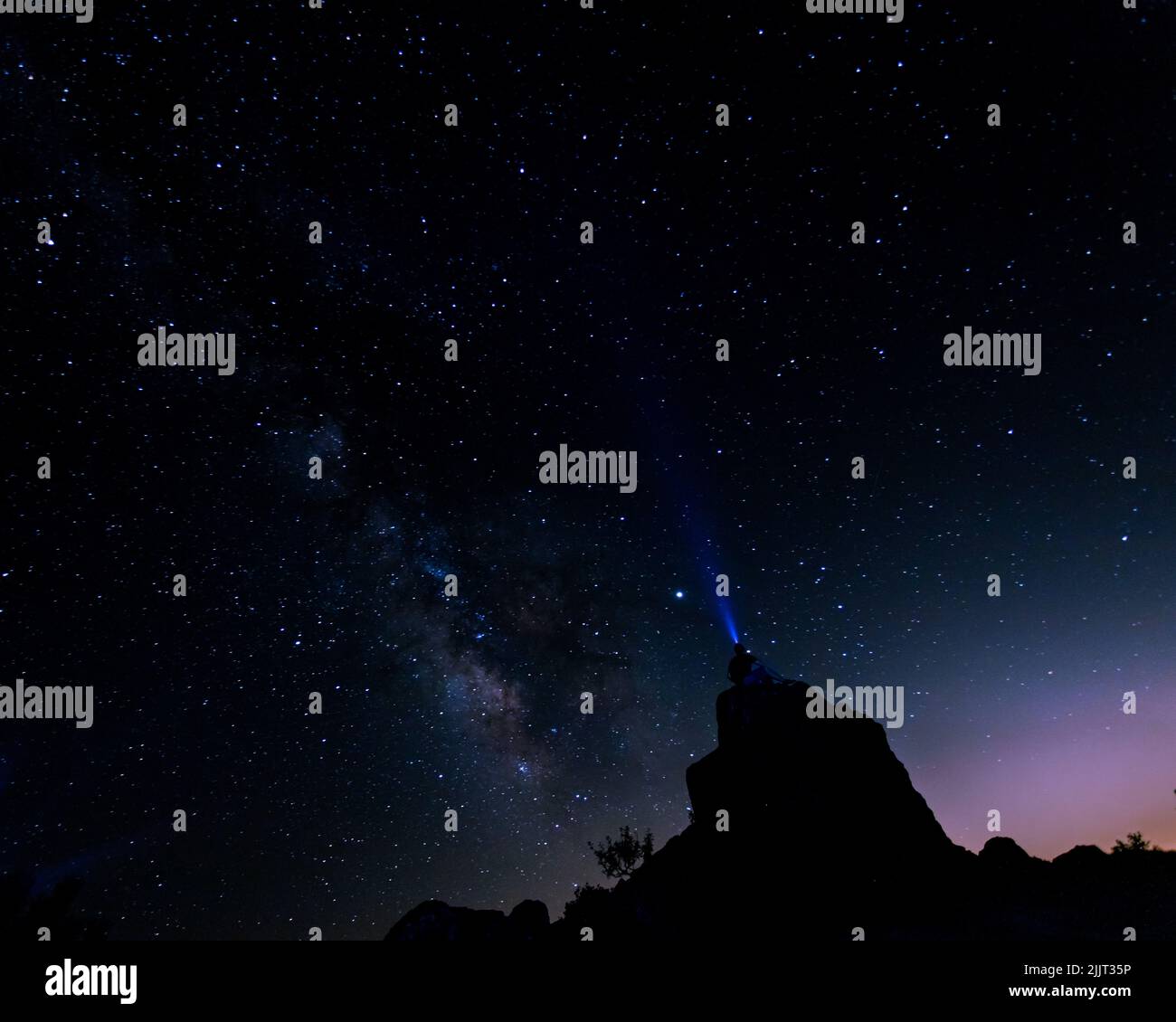 A silhouette of a person sitting on a peak and looking at the stars in ...