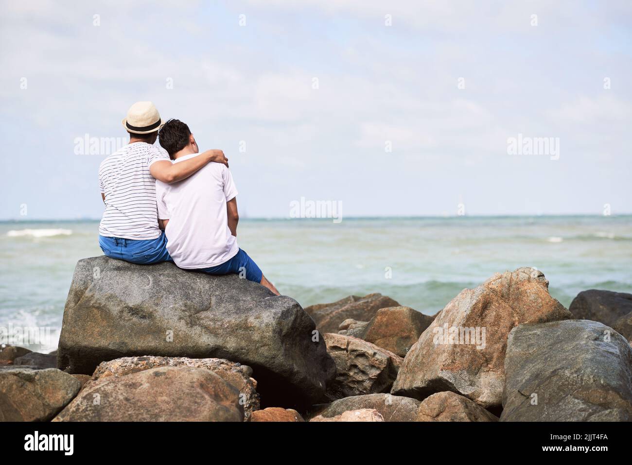 Hugging friends sitting on the rock by the water Stock Photo - Alamy