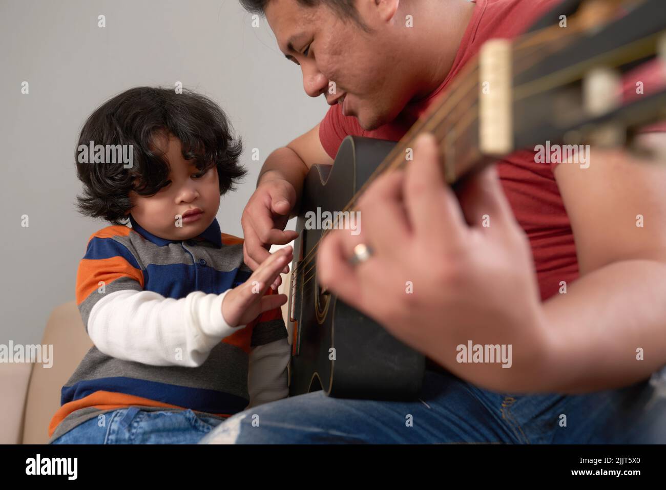 Asian man teaching his son how to play guitar Stock Photo - Alamy
