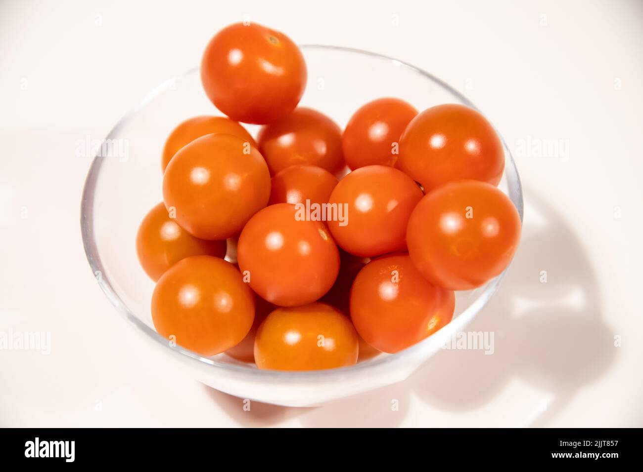 A heap of cherry tomatoes in a glass bowl isolated on white background ...