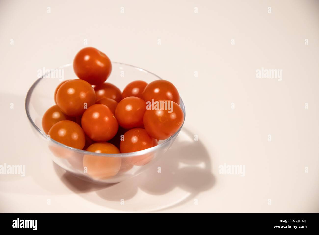 A heap of cherry tomatoes in a glass bowl isolated on white background ...