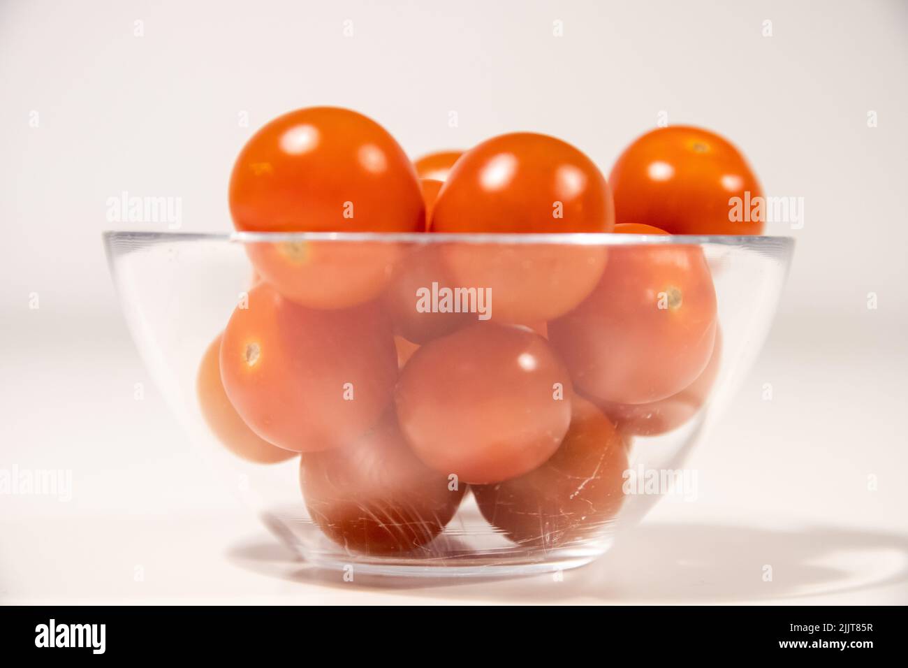 A heap of cherry tomatoes in a glass bowl isolated on white background ...