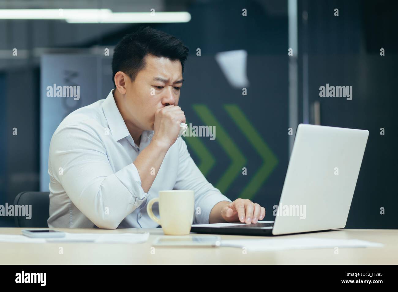 Sick at work. A young Asian businessman keeps coughing, covers his ...