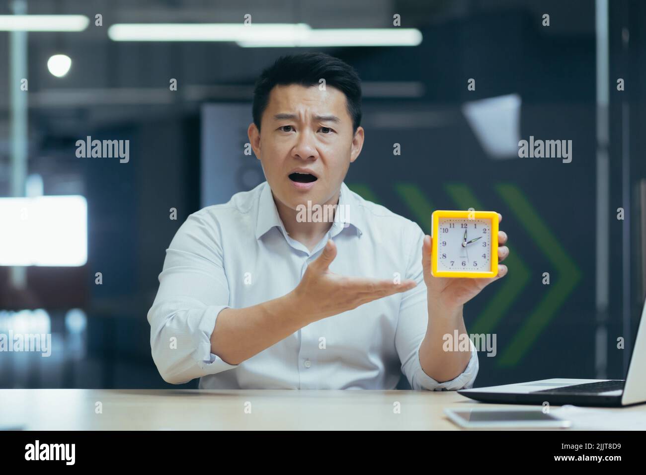 Time management. Young handsome asian businessman holding a desk clock ...