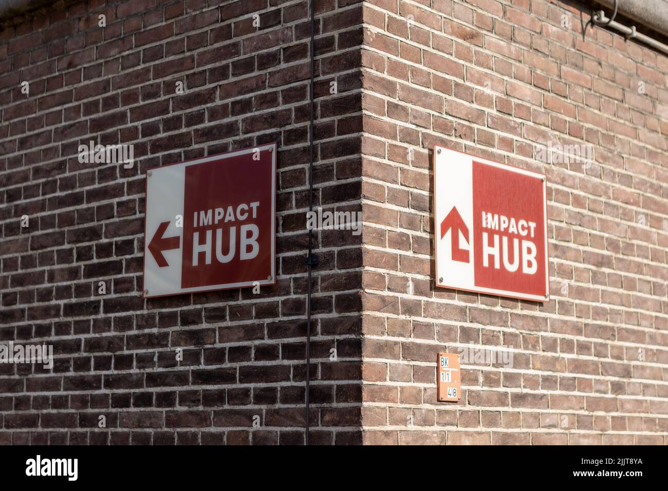 Signs on brick wall showing the way towards the Impact Hub in Dutch ...